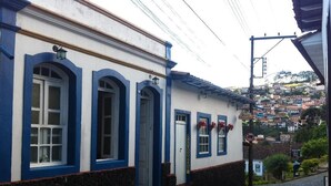 Uma rua de calçamento com um edifício com janelas em arco e uma porta, ao fundo uma cidade em colinas.