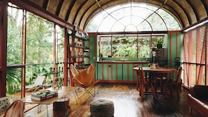 Um quarto com piso de madeira, uma mesa redonda, uma cadeira, um sofá e uma estante de livros.