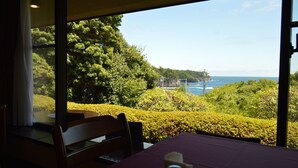 Uma sala de jantar com mesa posta para dois, com vista para um jardim exuberante e a costa.