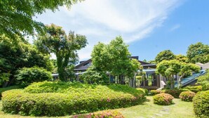 Um jardim bem cuidado, com sebes podadas e plantas floridas, cercado por edifícios modernos com grandes janelas.