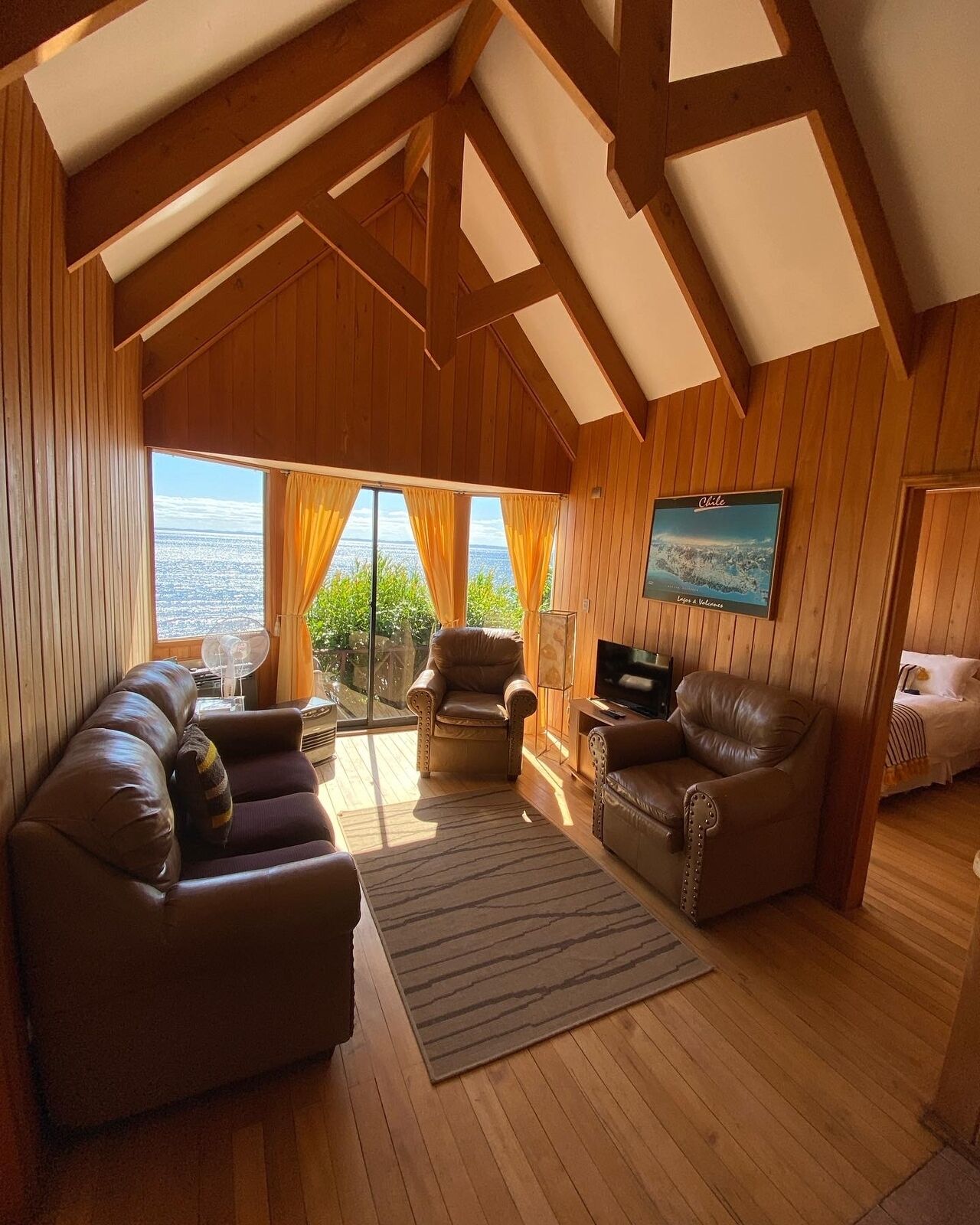 Uma sala de estar acolhedora com paredes de madeira e teto inclinado, com um sofá, poltronas e uma televisão.