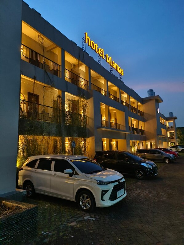 Um hotel com estrutura em vários andares, estacionamento externo e um letreiro grande com a palavra 'hotel'.