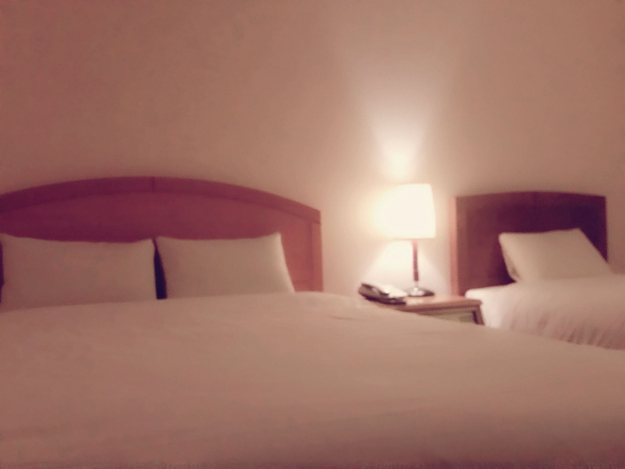 Quarto de hotel com uma cama grande, uma mesa de cabeceira com abajur e um telefone.