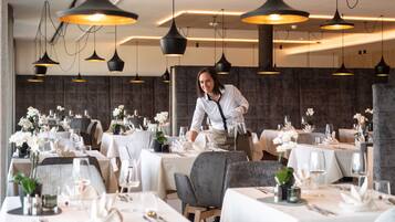 Restaurante com várias mesas preparadas para refeições, cada uma com toalhas brancas, copos de vinho e arranjos florais.