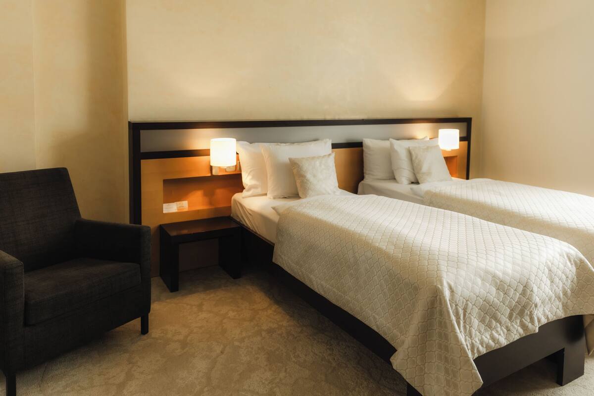 Quarto de hotel com duas camas de solteiro, uma poltrona e abajures.