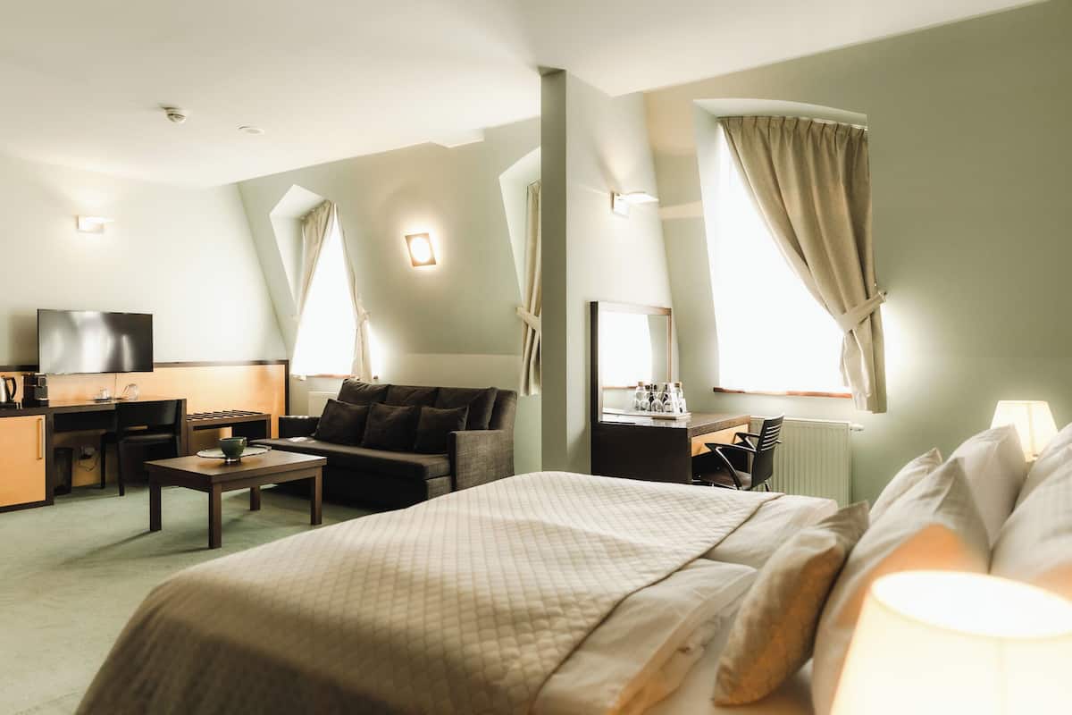 Quarto de hotel com cama, escrivaninha, cadeira, sofá e televisão.