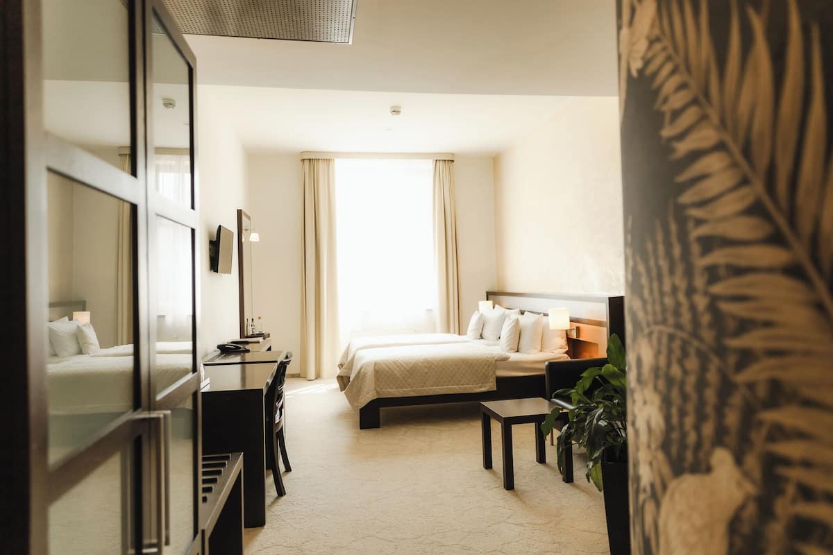 Quarto de hotel com cama, escrivaninha, cadeira, espelho e janela com cortinas.