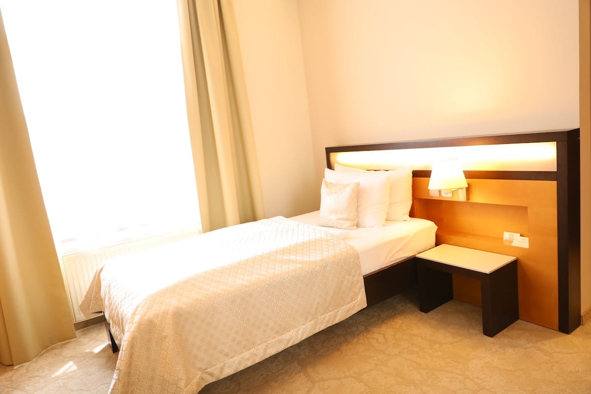 Quarto de hotel com cama, mesa de cabeceira, abajur e janela com cortinas.