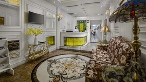 Um hall luxuoso com uma receção, um sofá, um candelabro e um padrão decorativo no chão.