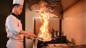 Um cozinheiro preparando comida em uma panela sobre um fogão com chamas.