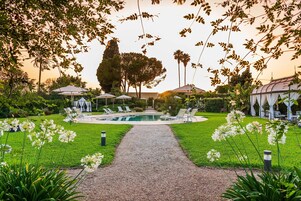 Um jardim com piscina, espreguiçadeiras e um gazebo.