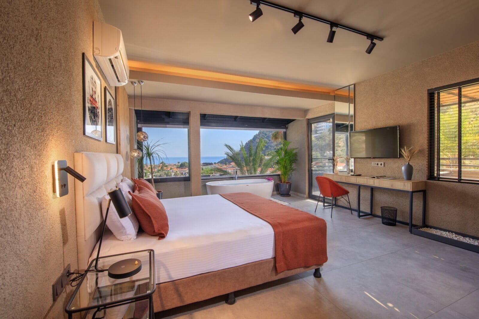 Quarto moderno com cama grande, escrivaninha, TV e vista para o mar.