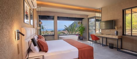 Quarto moderno com cama grande, escrivaninha, TV e vista para o mar.