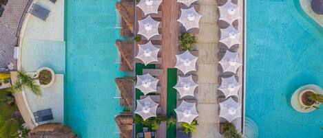 Vista aérea de um resort com uma piscina grande, espreguiçadeiras e guarda-sóis de palha.