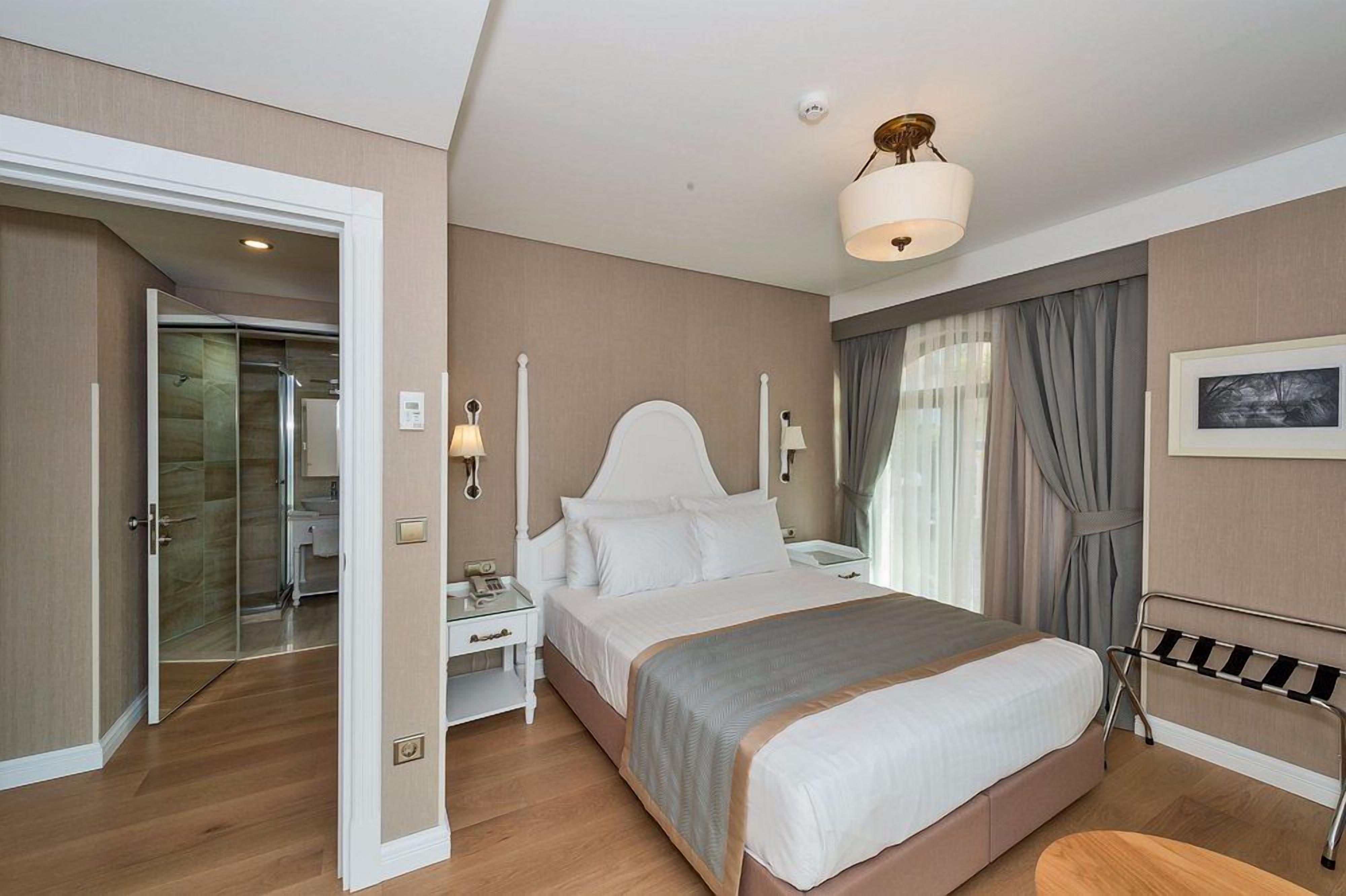 Quarto de hotel com cama, mesas de cabeceira, abajur, área de chuveiro e vista para o exterior.