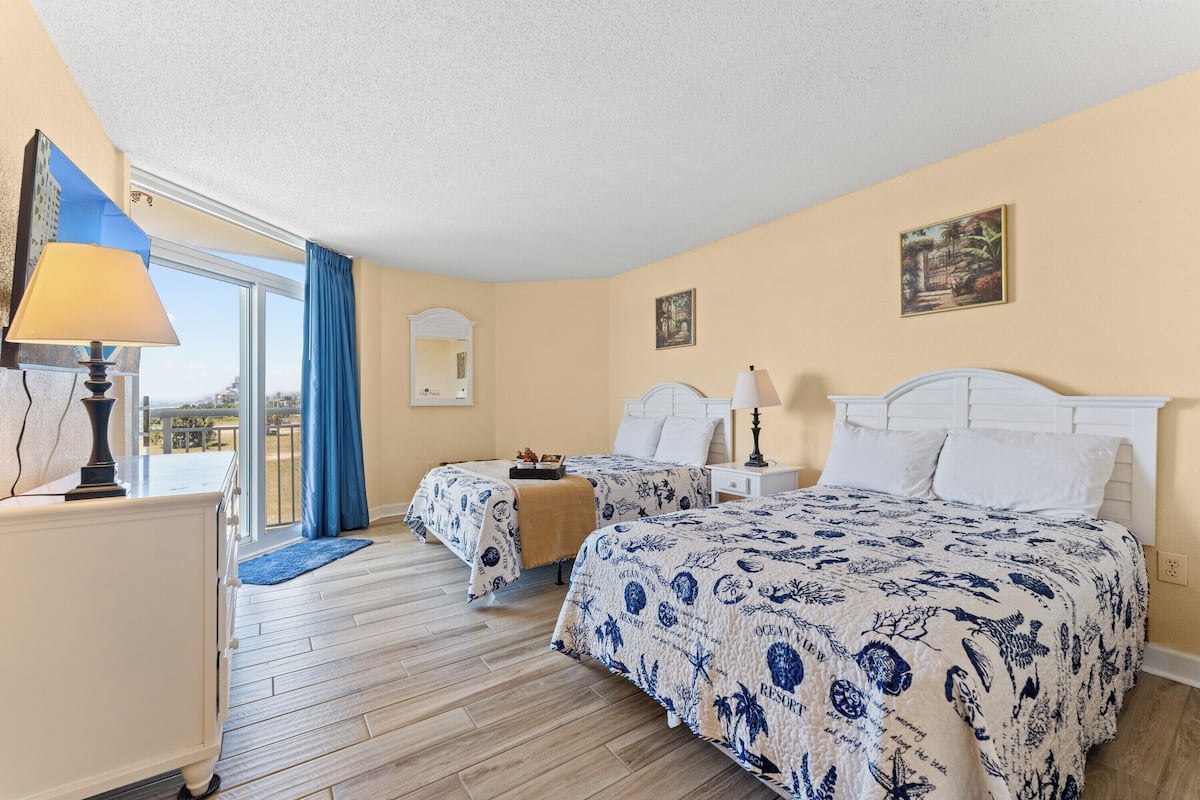 Quarto de hotel com duas camas, varanda, escrivaninha e uma cadeira.