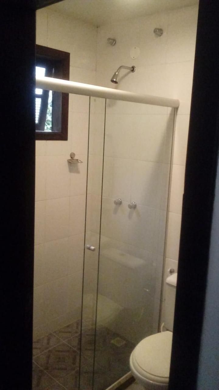 Box de chuveiro com paredes de vidro e uma casa de banho branca visível no espaço contíguo.