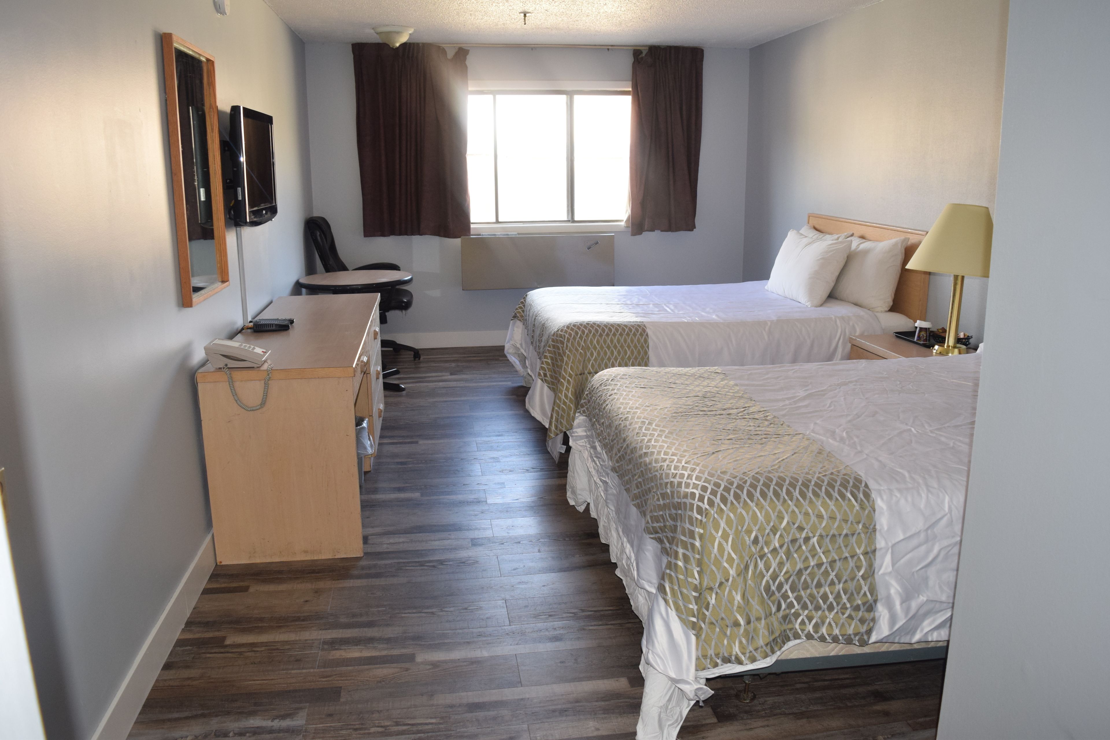 Quarto de hotel com duas camas, uma secretária com cadeira, televisão na parede e janela com cortinas.