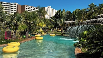 Uma área de piscina com toboáguas, boias infláveis e vegetação tropical.