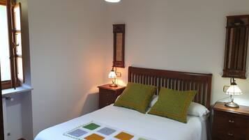 Cama bem arrumada com colcha colorida, cabeceira de madeira, duas luminárias de apoio e um espelho na parede.
