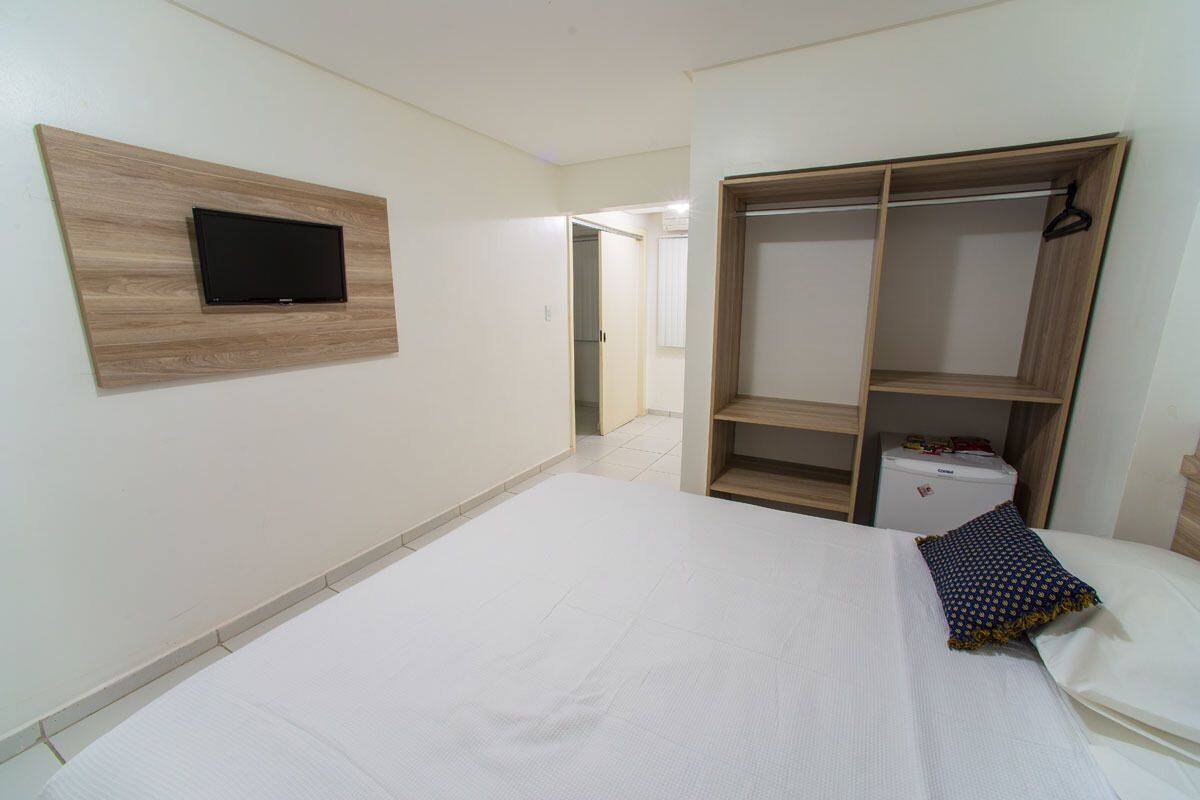 Quarto com cama, televisão na parede e armário.
