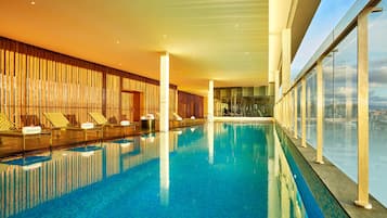 Uma grande piscina interna com espreguiçadeiras e uma parede de madeira.