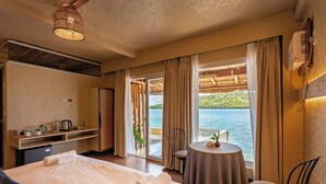 Quarto de hotel com cama, escrivaninha, cadeira, mesinha e vista para o mar.