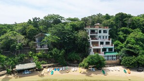 Imóvel à beira-mar com um edifício de vários andares, uma construção com telhado de palha e vários barcos na areia.