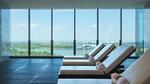 Espaço de relaxamento moderno em ambiente interno, com grandes janelas que dão para um corpo de água e vista da cidade.