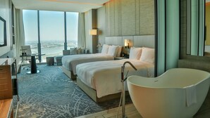 Quarto de hotel moderno com duas camas, uma banheira grande, uma escrivaninha e vista para a cidade.