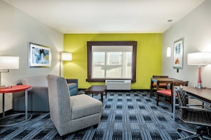 Quarto de hotel com sofá, poltrona, mesinha e escrivaninha com cadeiras.