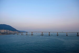 Uma longa ponte sobre a água, com um horizonte urbano e montanhas ao fundo.