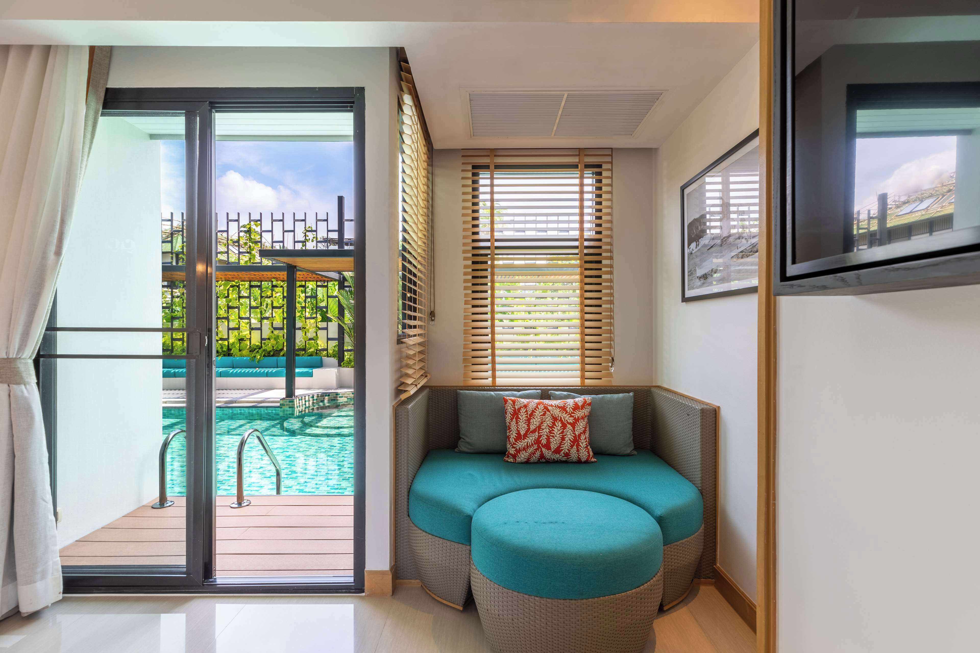 Quarto com porta de vidro deslizante para uma piscina, área de estar com assentos acolchoados e vista, e televisão montada na parede.
