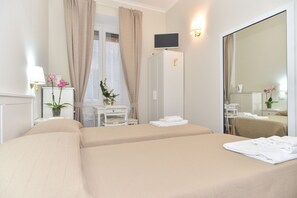 Quarto de hotel com duas camas, uma escrivaninha com cadeira, uma televisão e um espelho grande.