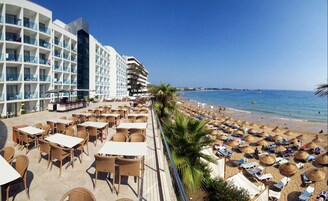 Um hotel à beira-mar com área de estar externa e guarda-sóis, espaço com piscina e vista para a praia e oceano.
