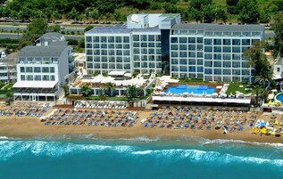 Um hotel na praia com vários edifícios, uma ampla área de piscina e muitos espreguiçadeiras na areia.