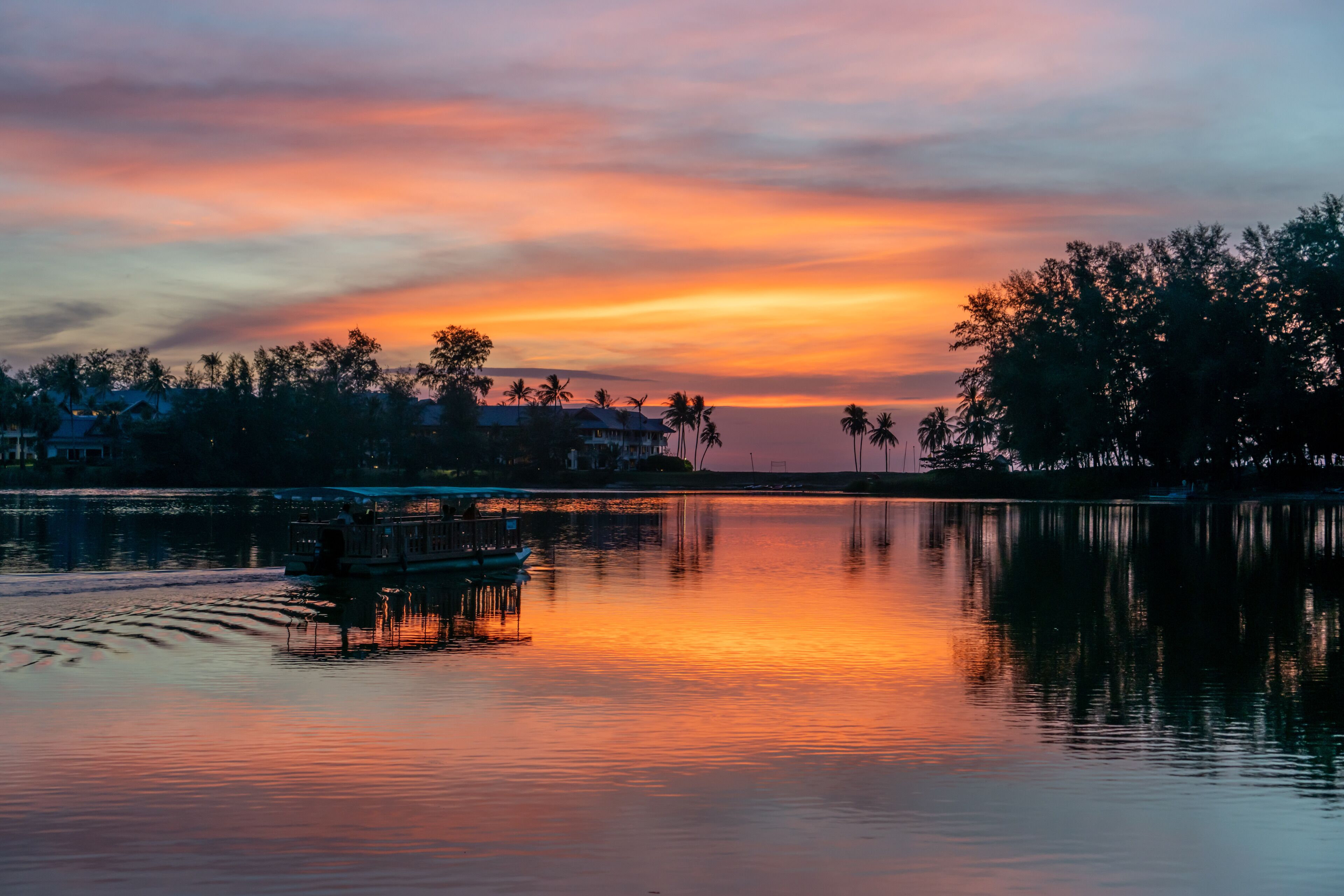 Um lago calmo ao pôr do sol, com um barco em primeiro plano e uma fileira de casas ao longo da margem.