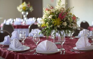 Uma mesa de banquete posta com guardanapos brancos, copos de vinho e um arranjo central de flores variadas.