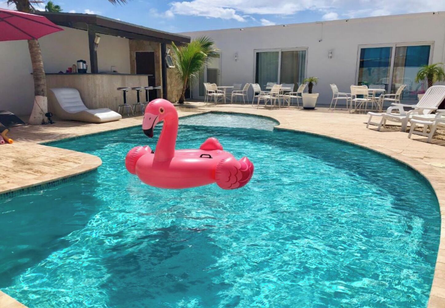 Piscina com boia de flamingo rosa, espreguiçadeiras e um edifício moderno ao fundo.