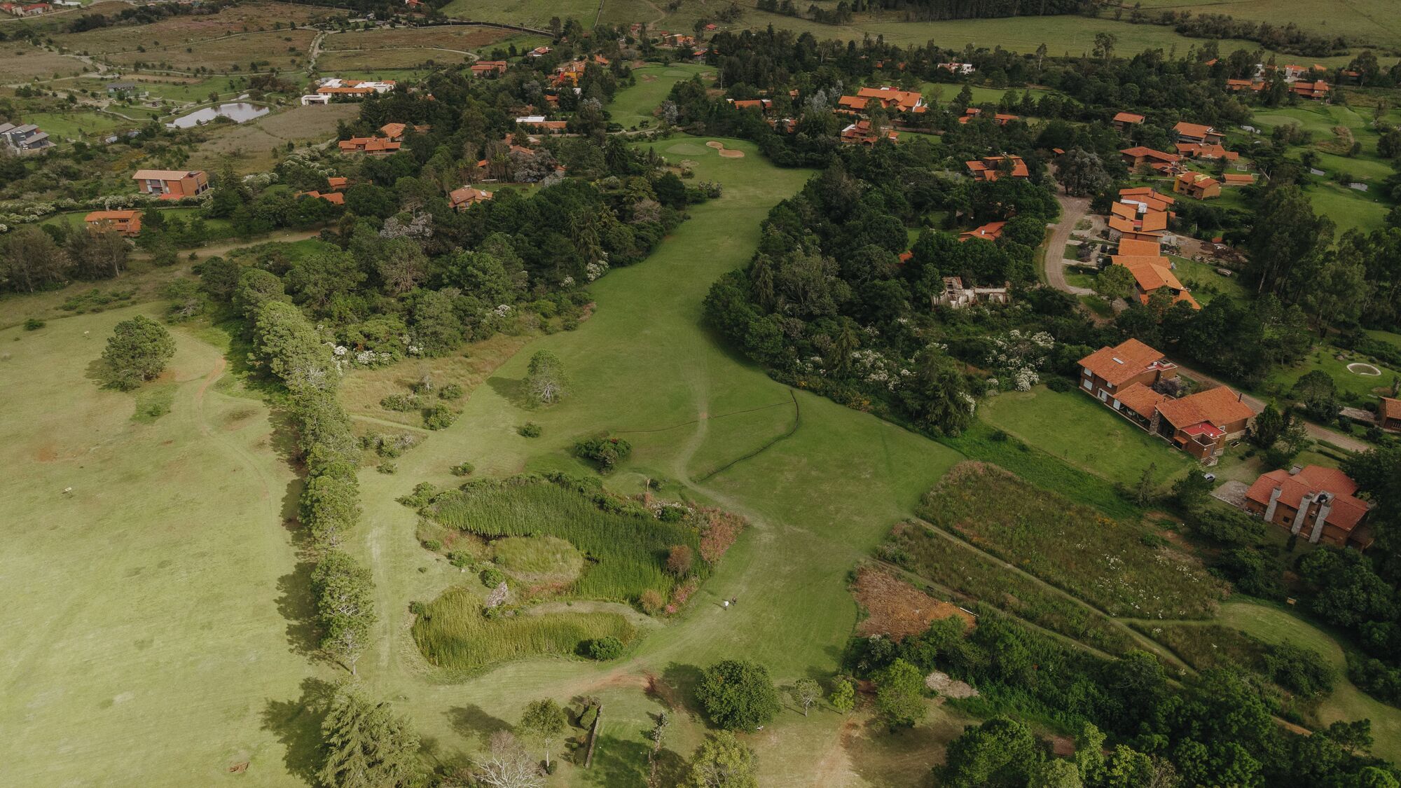 Vista aérea de uma área residencial com casas, campos verdes e um campo de golfe.