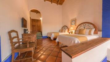Um quarto com uma escrivaninha de madeira, duas camas, uma cadeira e chão de azulejos.