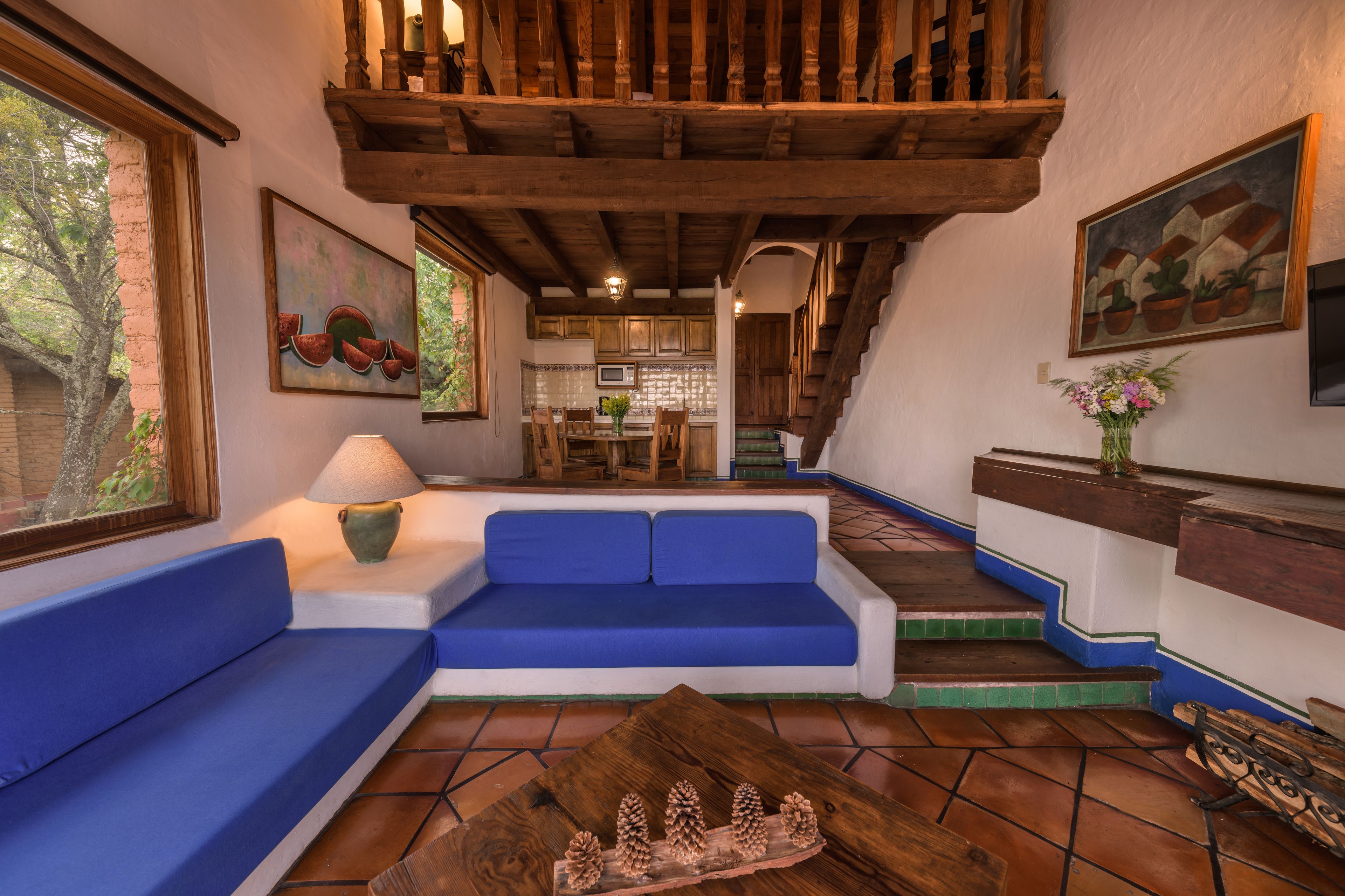 Uma sala de estar com um sofá azul, mesa de centro de madeira e uma escada que leva a um andar superior.