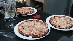 Um forno a pizza, duas pizzas em pratos, uma taça de vinho e um saleiro sobre uma mesa.