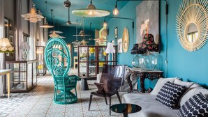 Quarto com paredes verde-água, um sofá, cadeiras e luminárias pendentes.