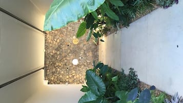 Pátio com parede de pedra, plantas verdes grandes e grade de metal.