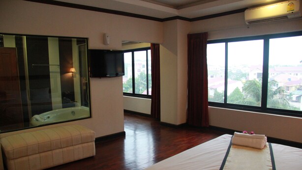 Quarto de hotel com uma cama grande, um banco, uma TV e uma janela com vista para a cidade.