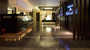 Um hall de hotel moderno com piso de mármore polido, balcão de recepção e uma placa de 'Welcome'.