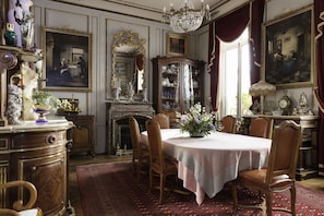 Uma sala de jantar formal com uma mesa redonda, cadeiras, um candelabro e uma lareira.