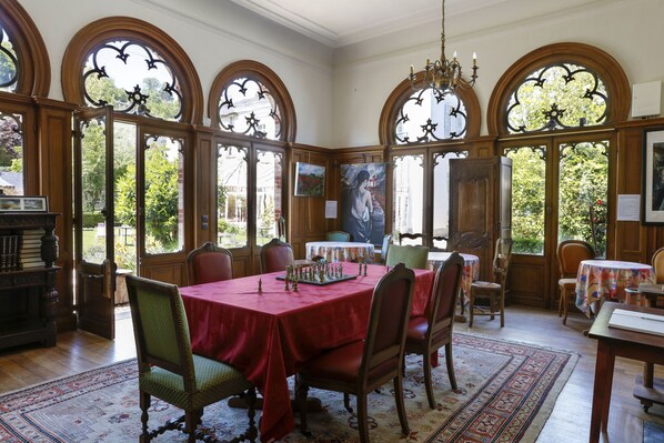 Uma área de refeições com toalha de mesa vermelha, cadeiras de madeira e um tabuleiro de xadrez.