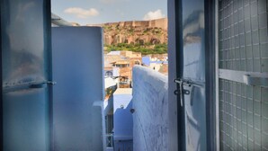 Vista através de uma porta aberta com portão de metal, dando para um pátio com edifícios e uma colina rochosa ao fundo.